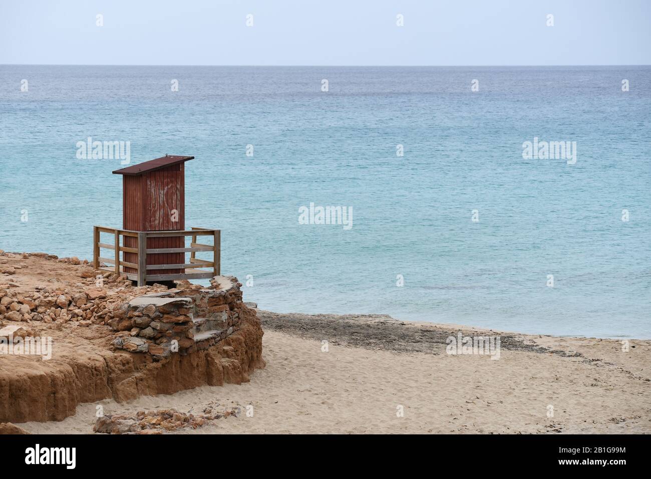 A brown wooden lifeguard house in an empty beach with clear blue sea in ...