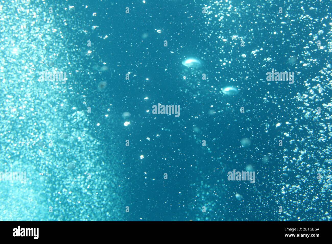 Blue ocean waves from underwater with bubbles. Light rays shining ...