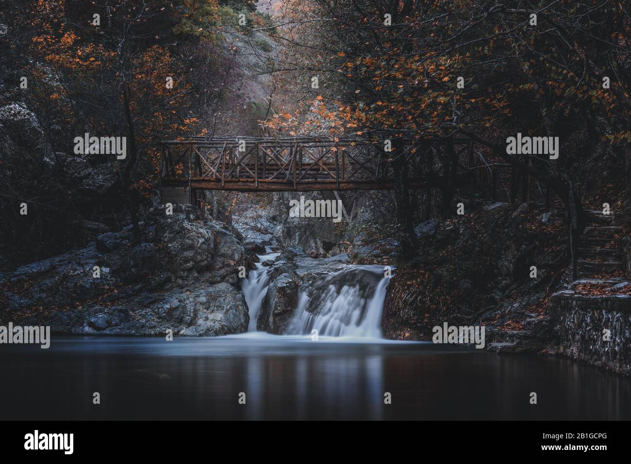 A small waterfall in a small lake under a wooden bridge. The water ...