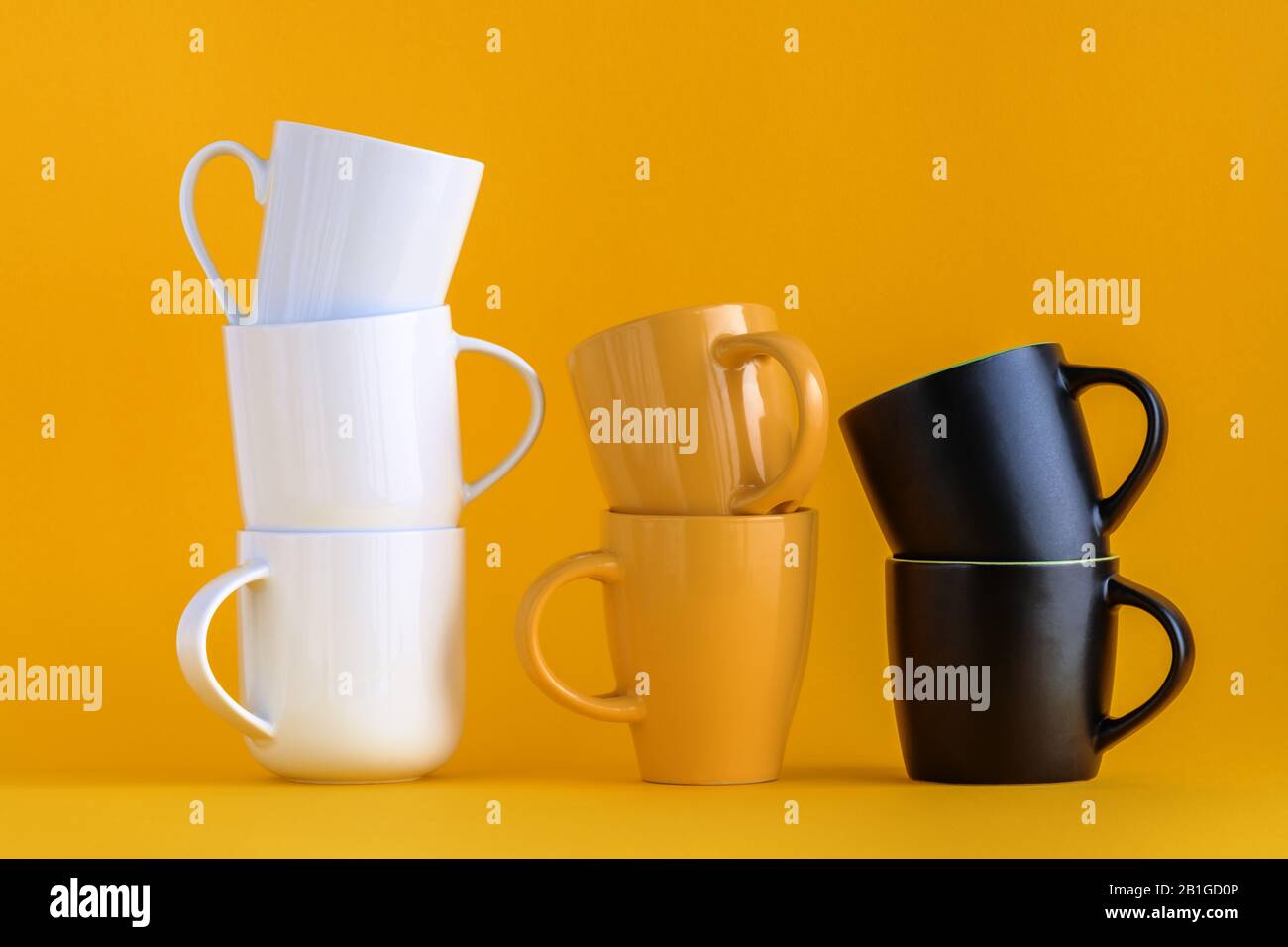 White, black and yellow coffee cups stack on yellow background with ...