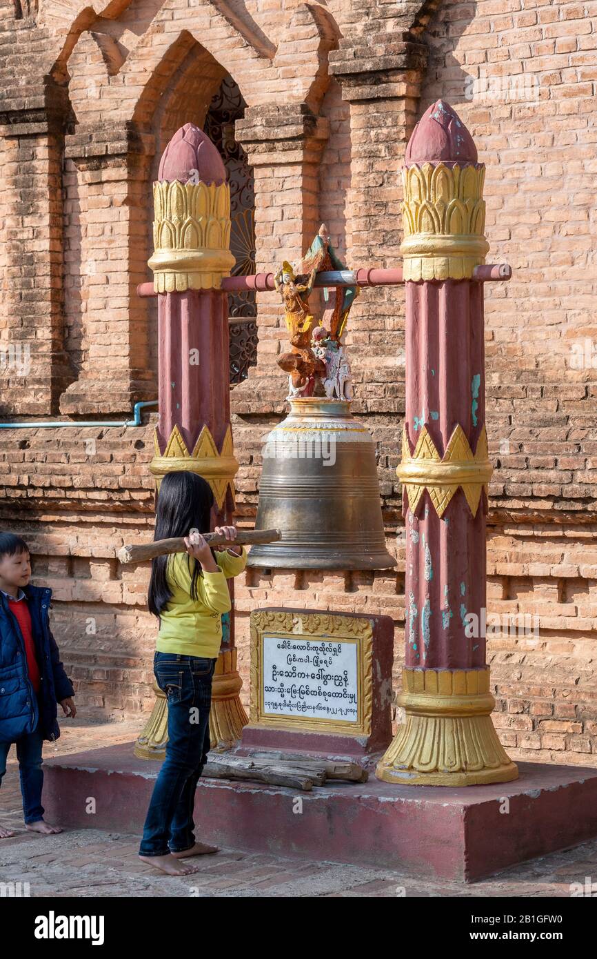 Young Burmese children strking ceremonial bell at Myazedi Pagoda, Bagan ...