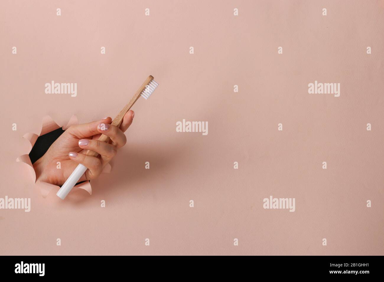 Wooden toothbrush in a female hand through round hole in pink paper ...