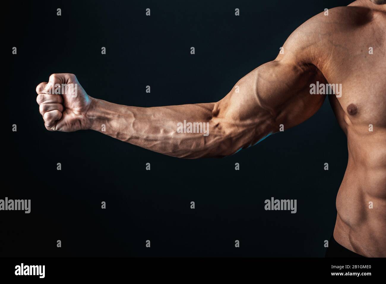 tense arm clenched into fist, veins, bodybuilder muscles on a dark ...