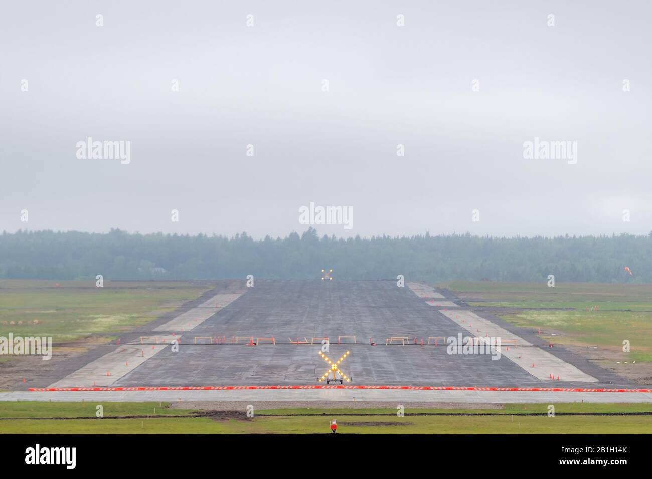 Closed runway at an airport on an overcast, foggy day. The runway has a ...
