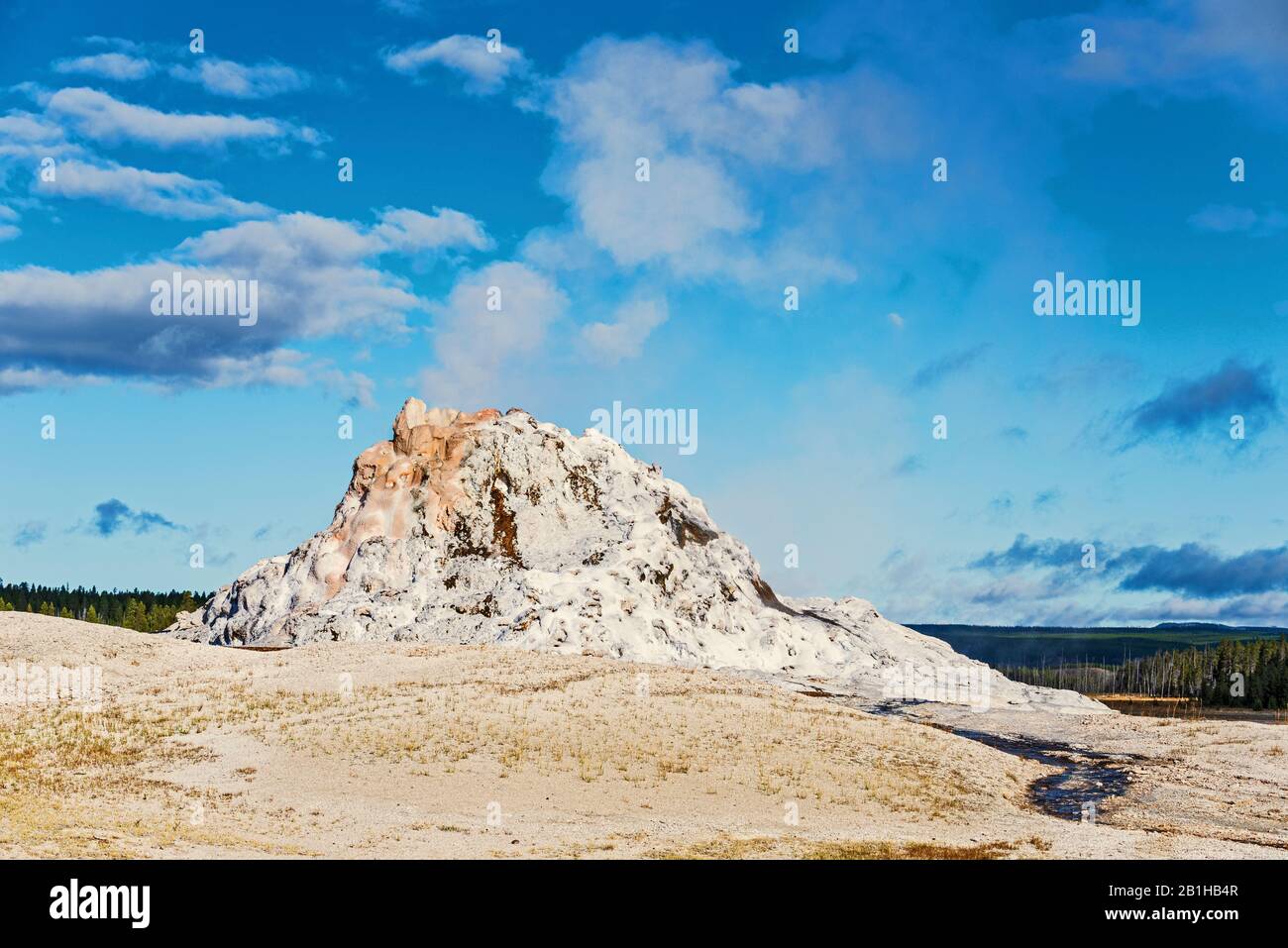 Steaming geyser rock formation against a blue sky with white clouds ...
