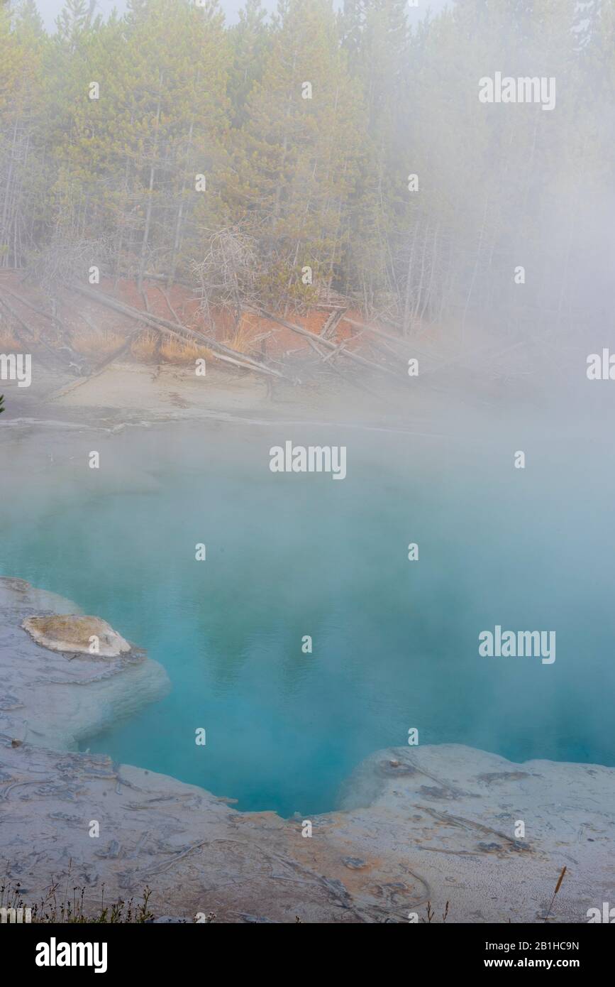 Bright blue hot spring on cold morning making a foggy scene. Shore and ...