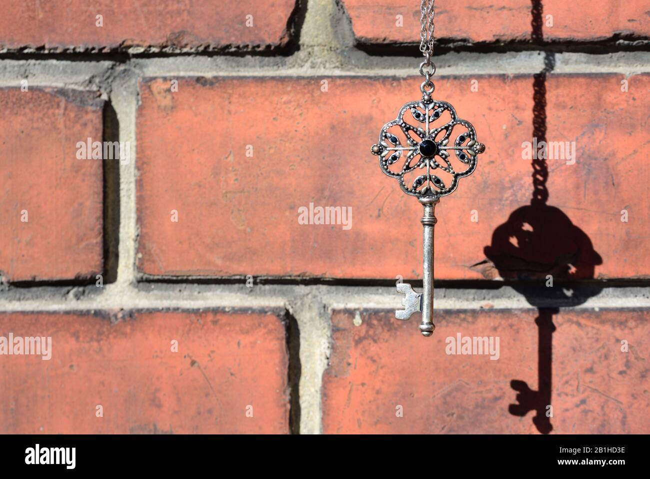 An old antique metal key hangs on a silver chain in front of a brick ...