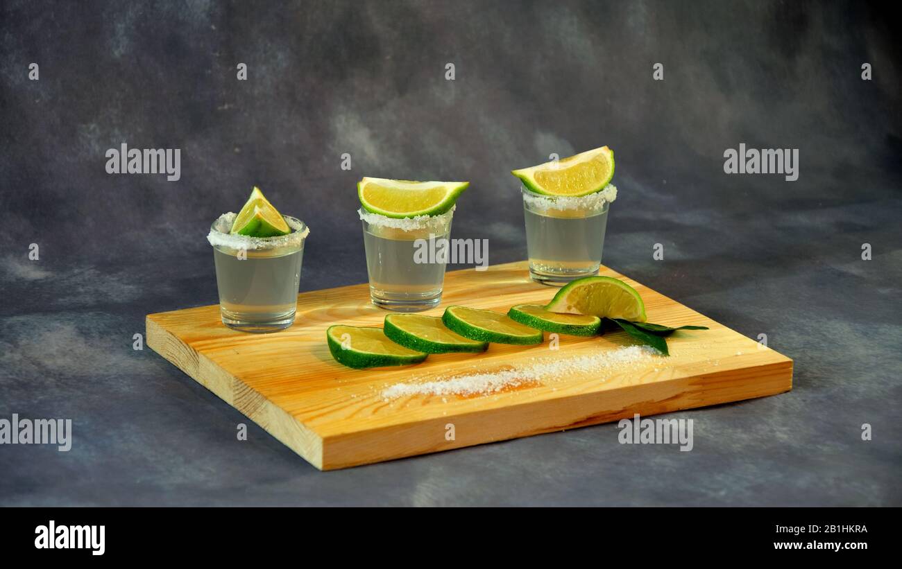 Wooden stand with three glasses of tequila, lime slices and salt on a ...