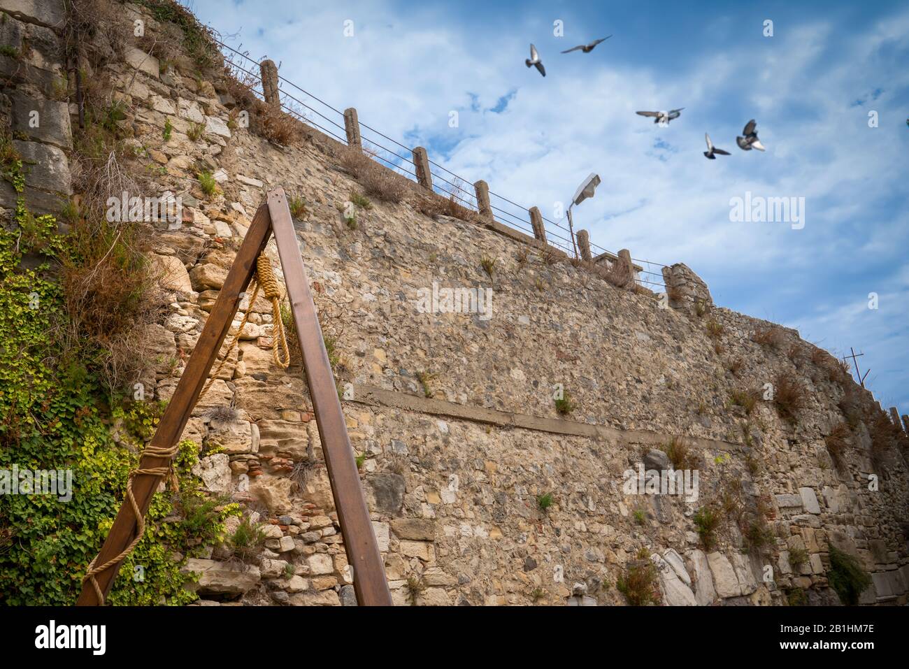 The gallows near stone wall and and blurred birds in sky. Concept of ...