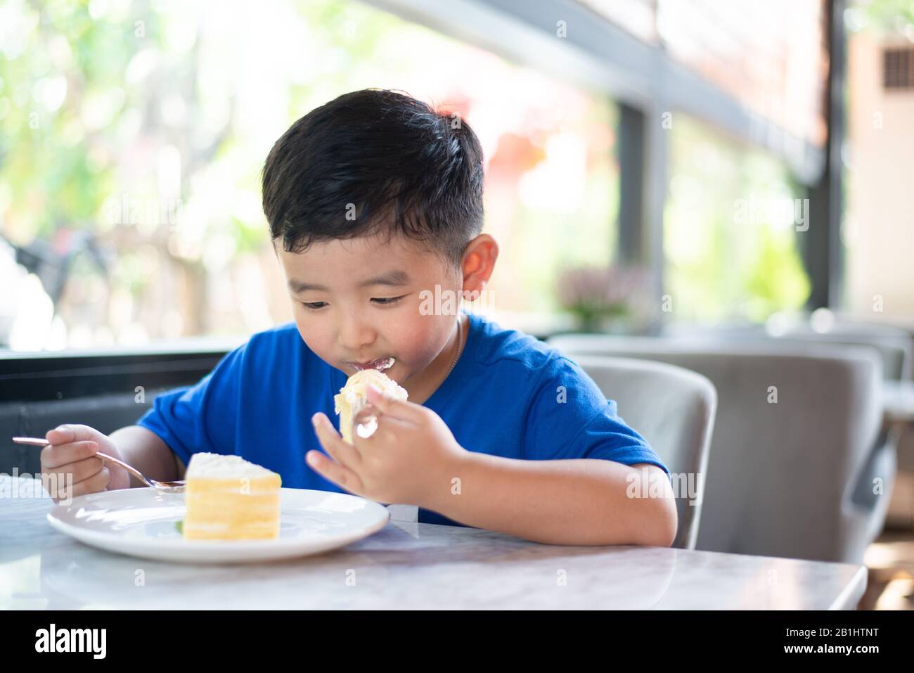 Cute little Asian boy eating cake in bakery shop or cafe Stock Photo ...