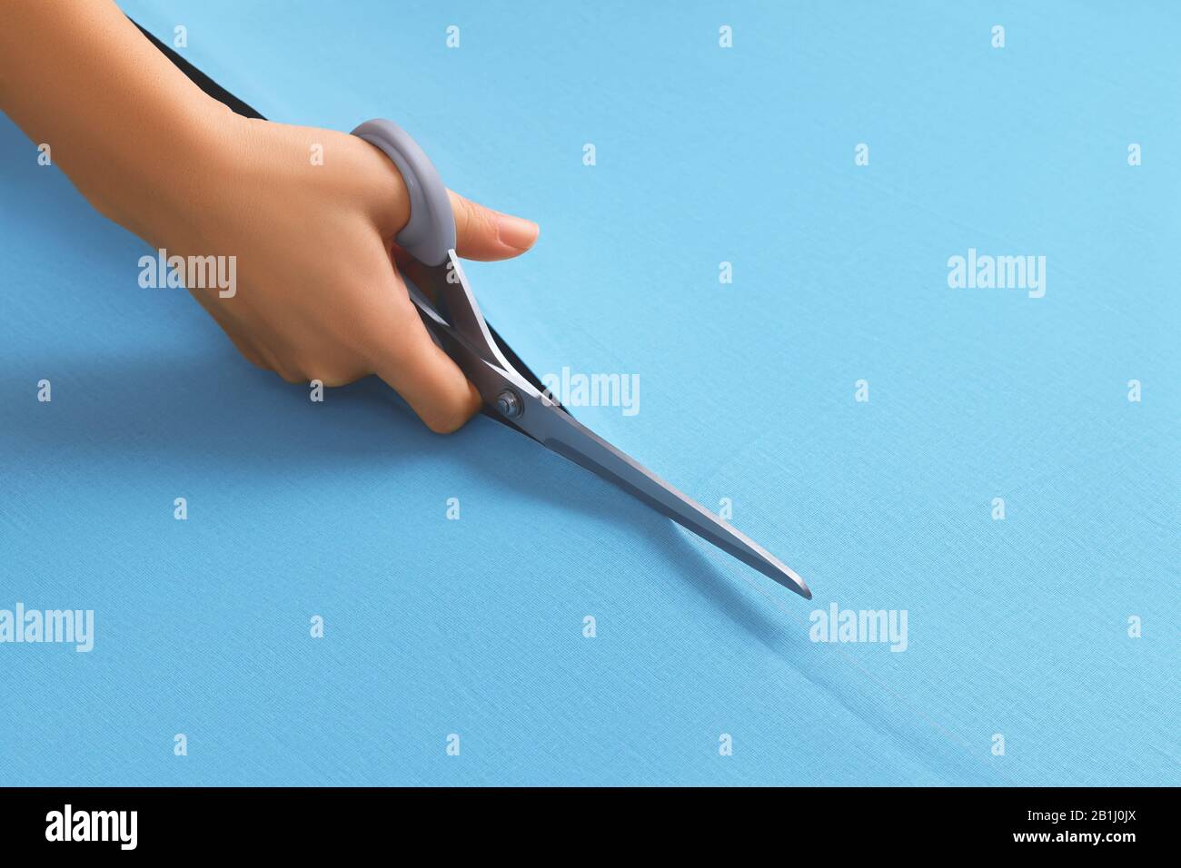 The hand of a young girl seamstress holds scissors and cuts smooth blue ...