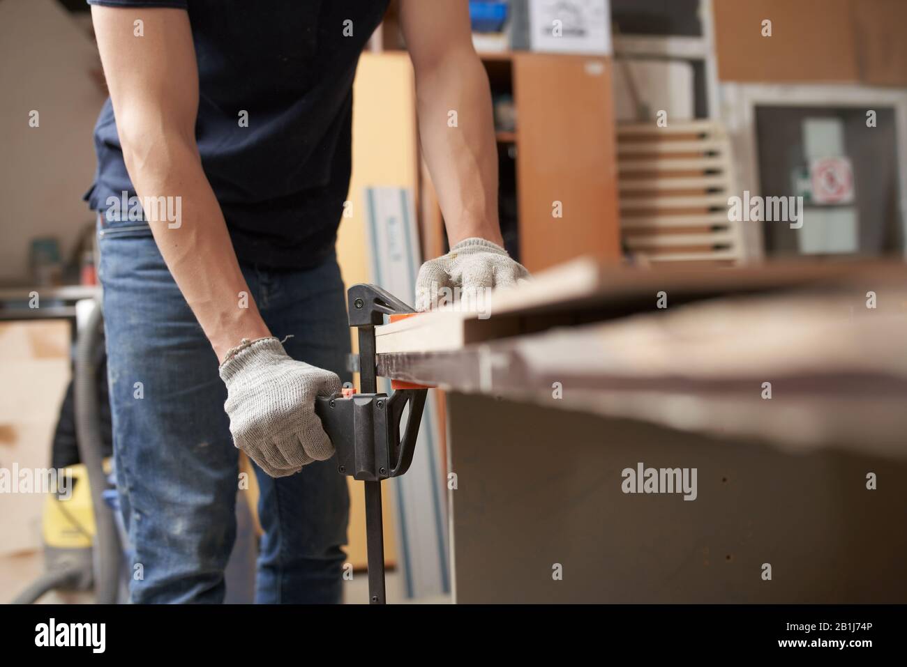 Male carpenter in gloves clamps board in vice at workshop , close-up ...
