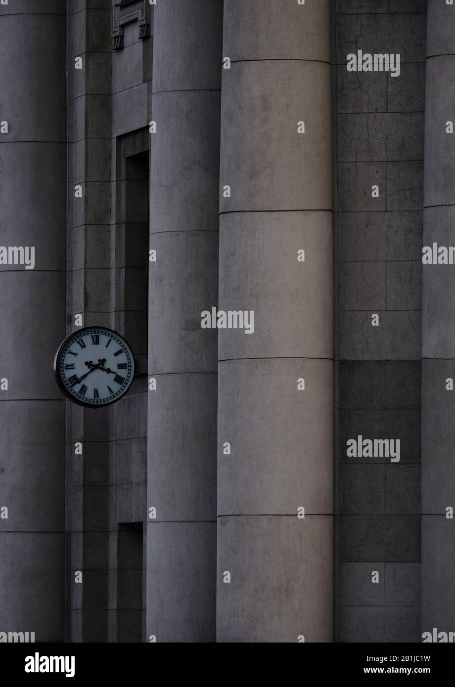 Clock hanging on a building with concrete columns and a facade Stock ...