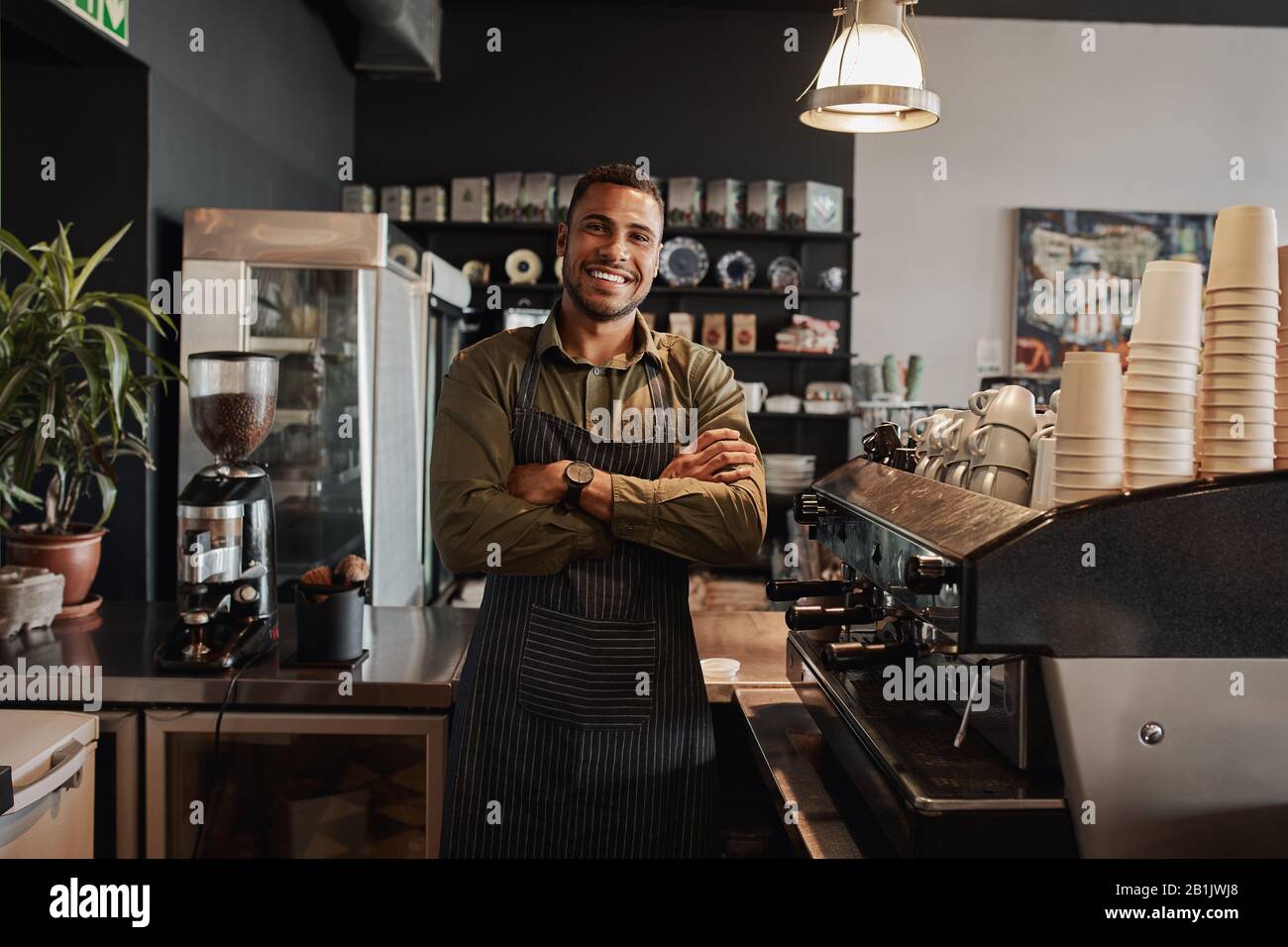 Portrait of a smiling confident young waiter standing at the cafe ...
