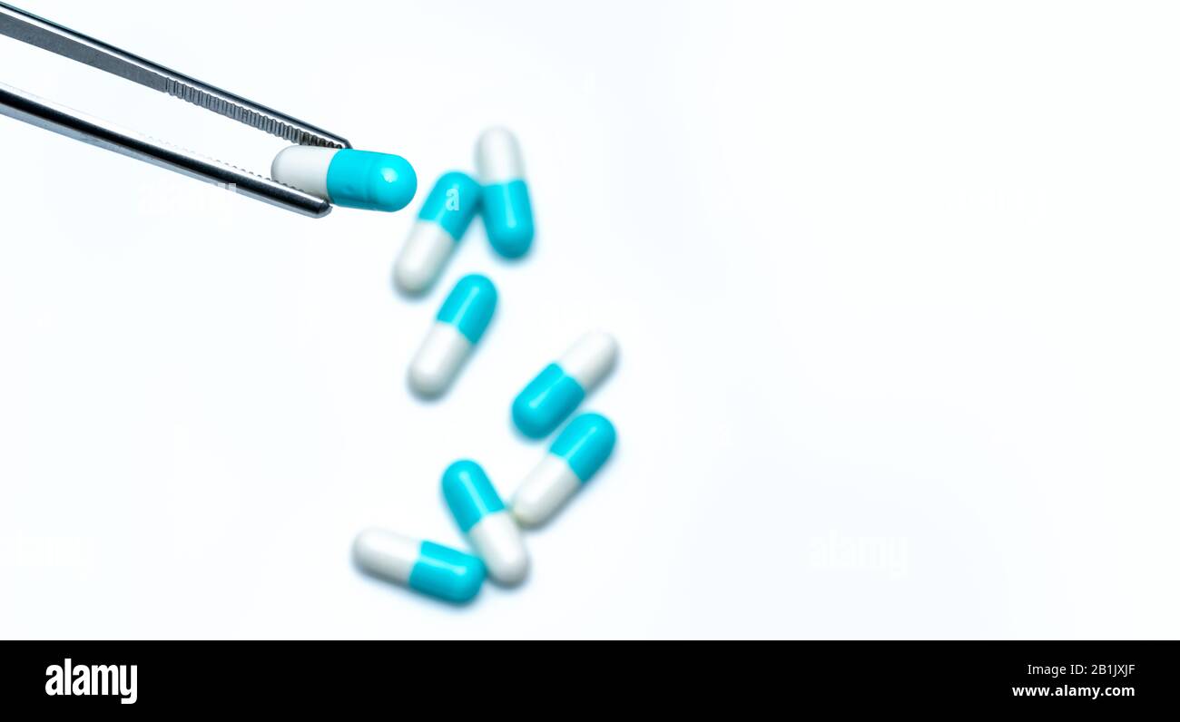 Forceps pick white-blue capsule from group of capsule pills. Drugs ...