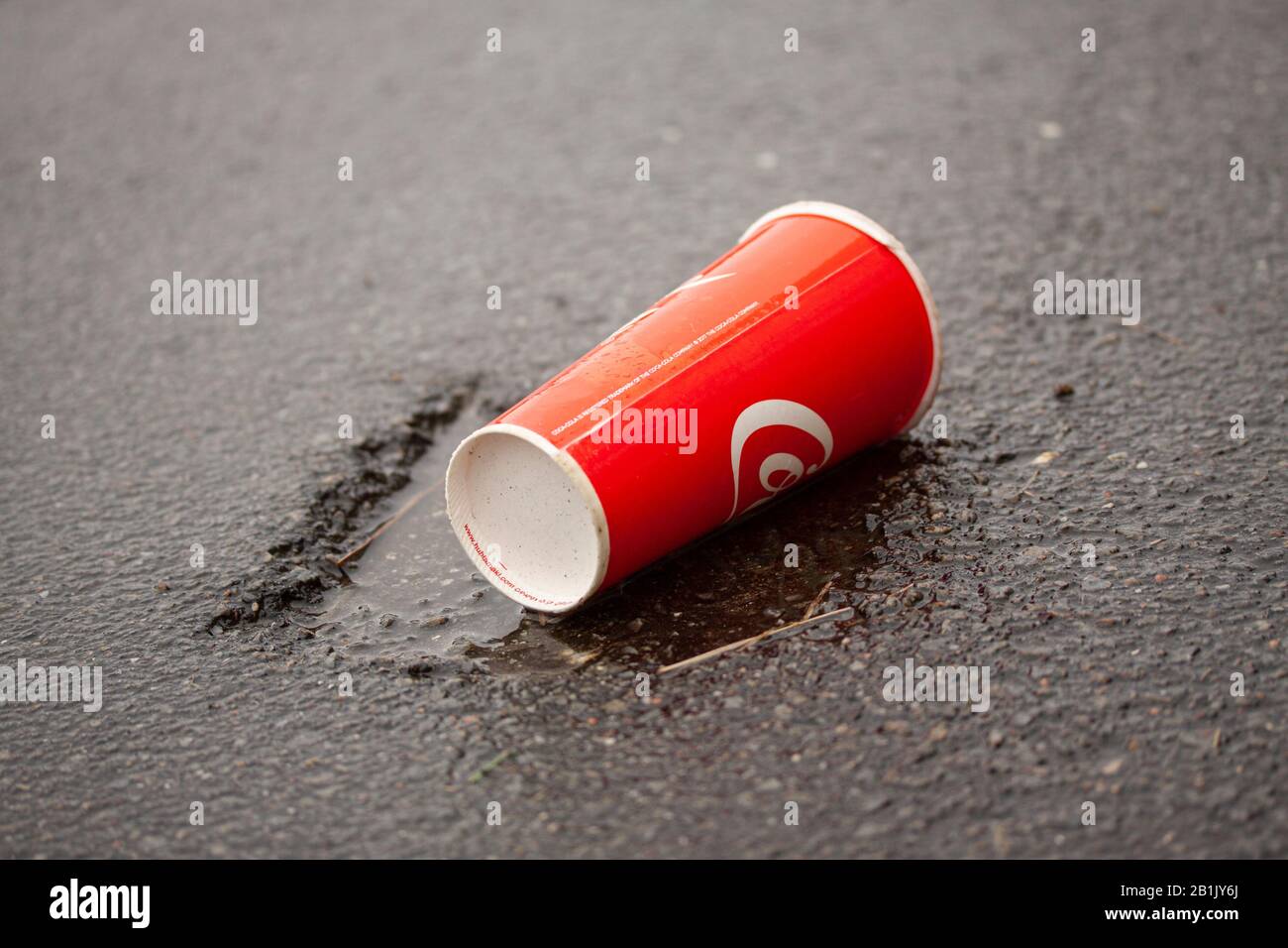 Coca Cola soda cup thrown on ground on asphalt road. Plastic wast ...