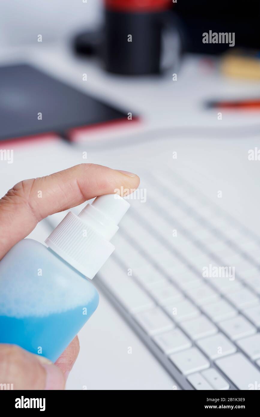 closeup of a caucasian man disinfecting a computer keyboard by spraying ...