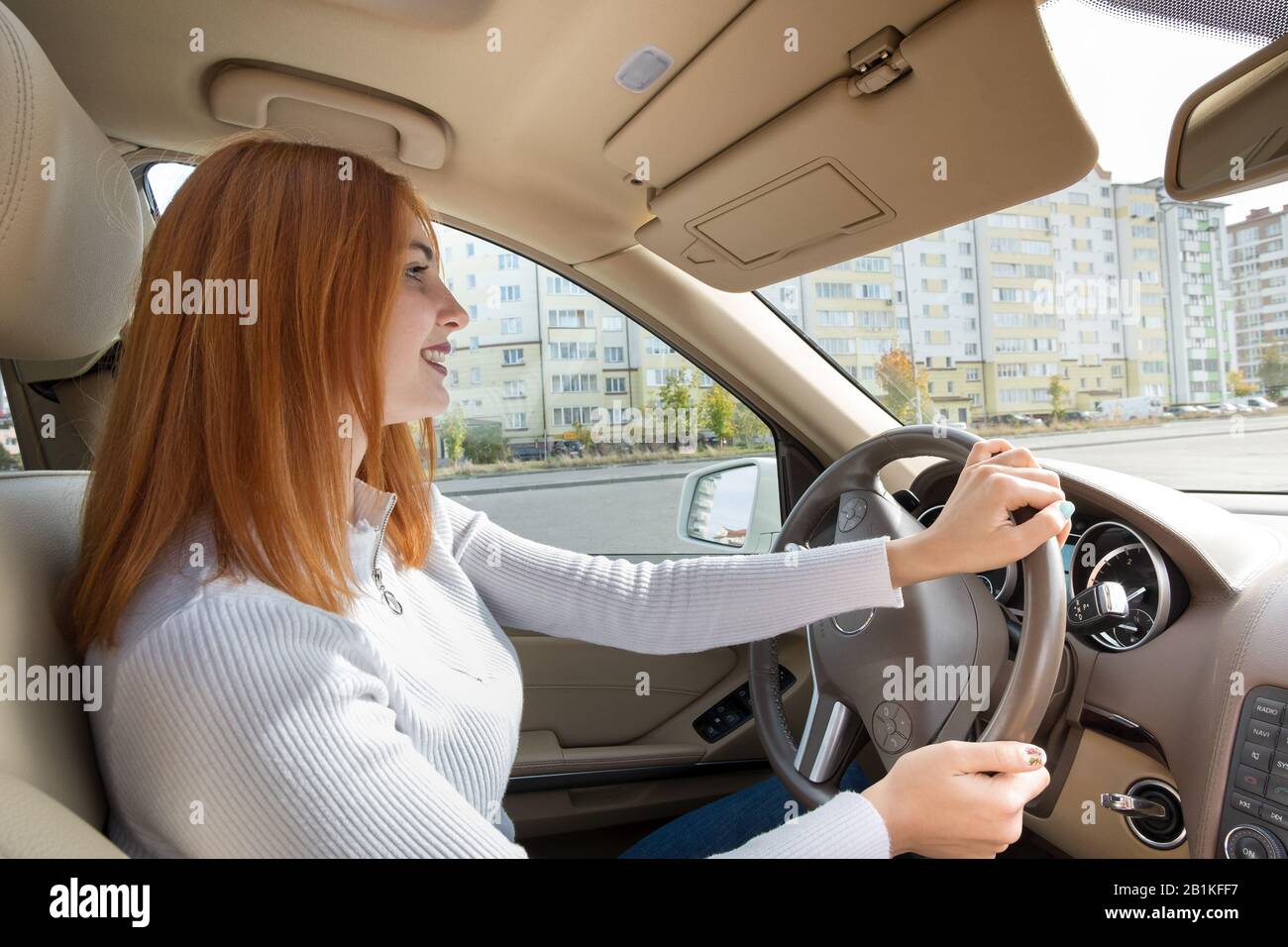 Young redhead woman driver behind a wheel driving a car smiling happily ...