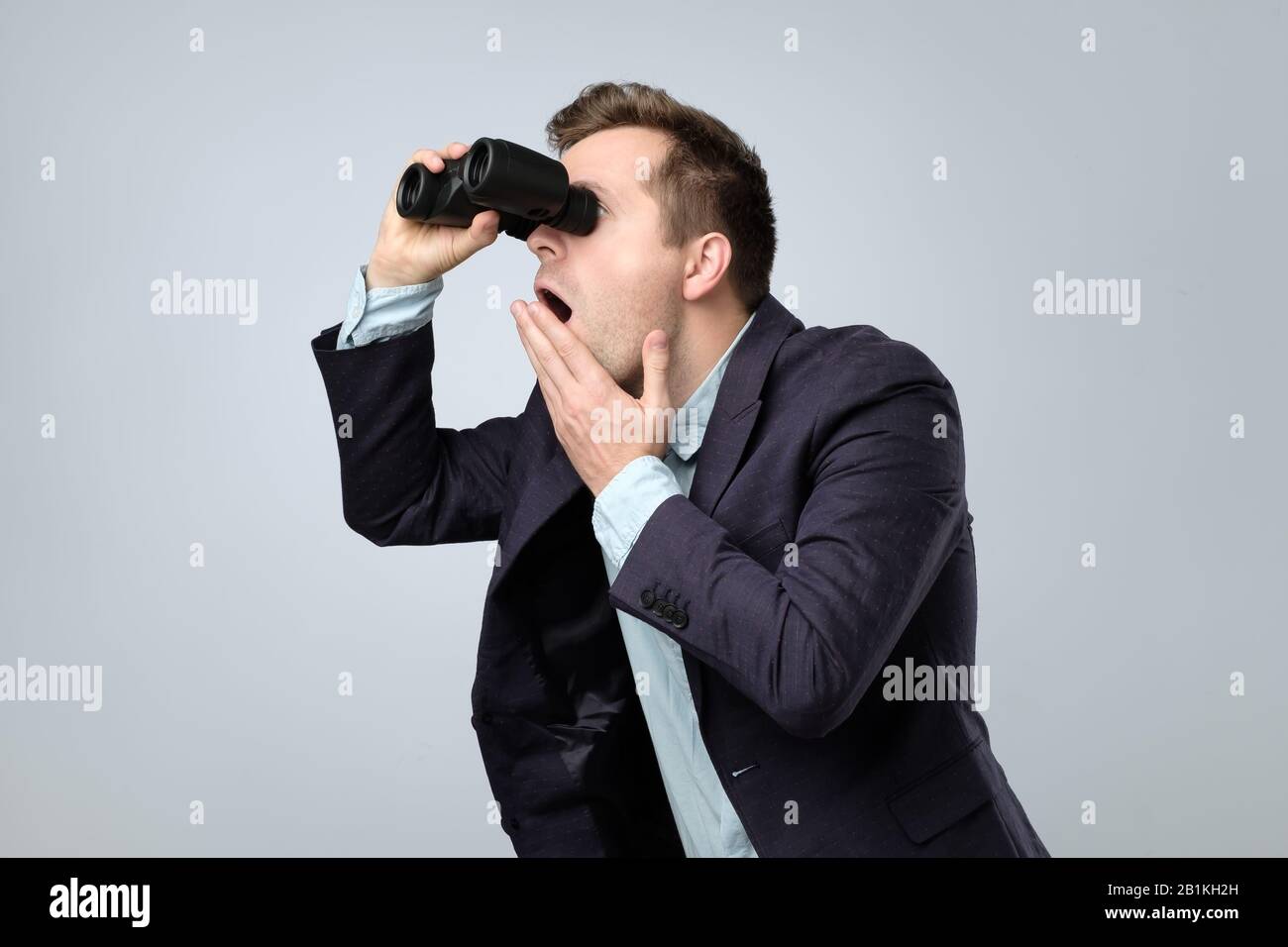 Young shocked businessman looking to the future through binoculars ...
