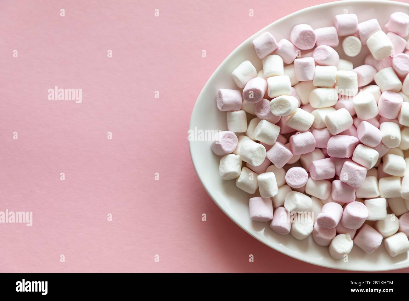 Pink and white mini marshmallows in white plate on pink background with ...