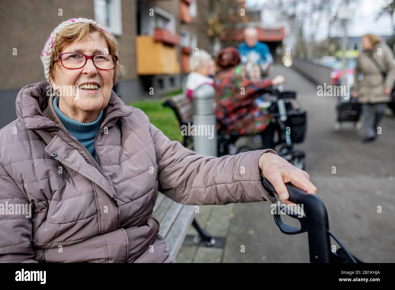 Senior citizen sitting on a bench in front of a residential building ...