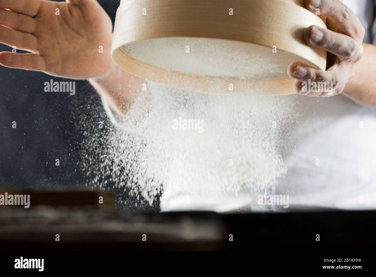 Male hands of a cook sifting flour through a sieve in the kitchen side ...