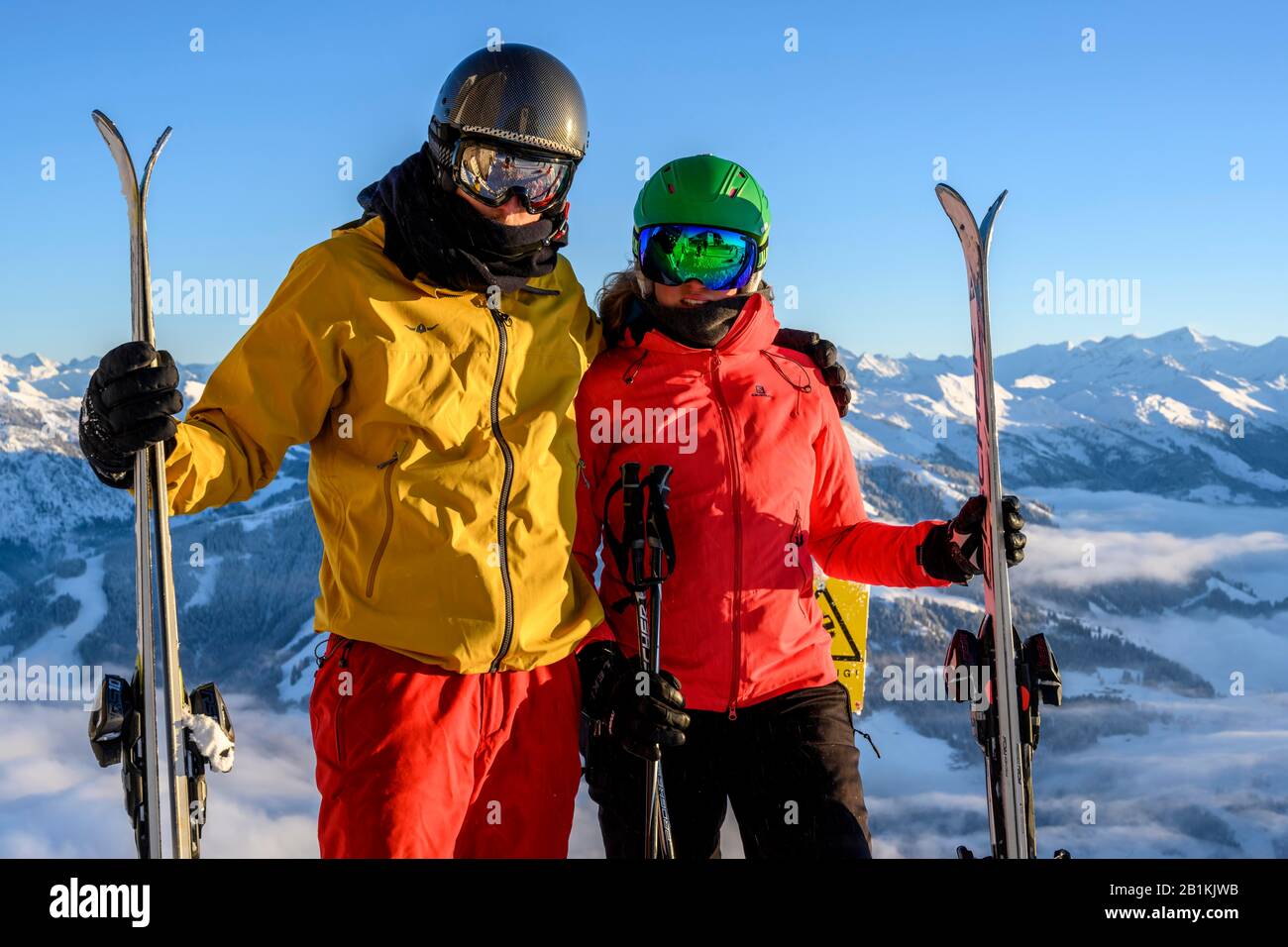 Two skiers with ski helmets and skis stand in front of a mountain ...