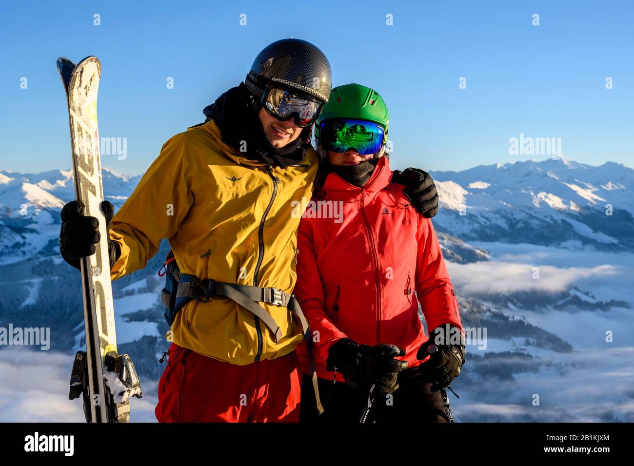 Two skiers with ski helmets and skis stand in front of a mountain ...