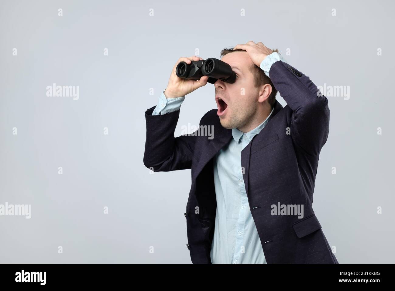 Young shocked businessman looking to the future through binoculars ...