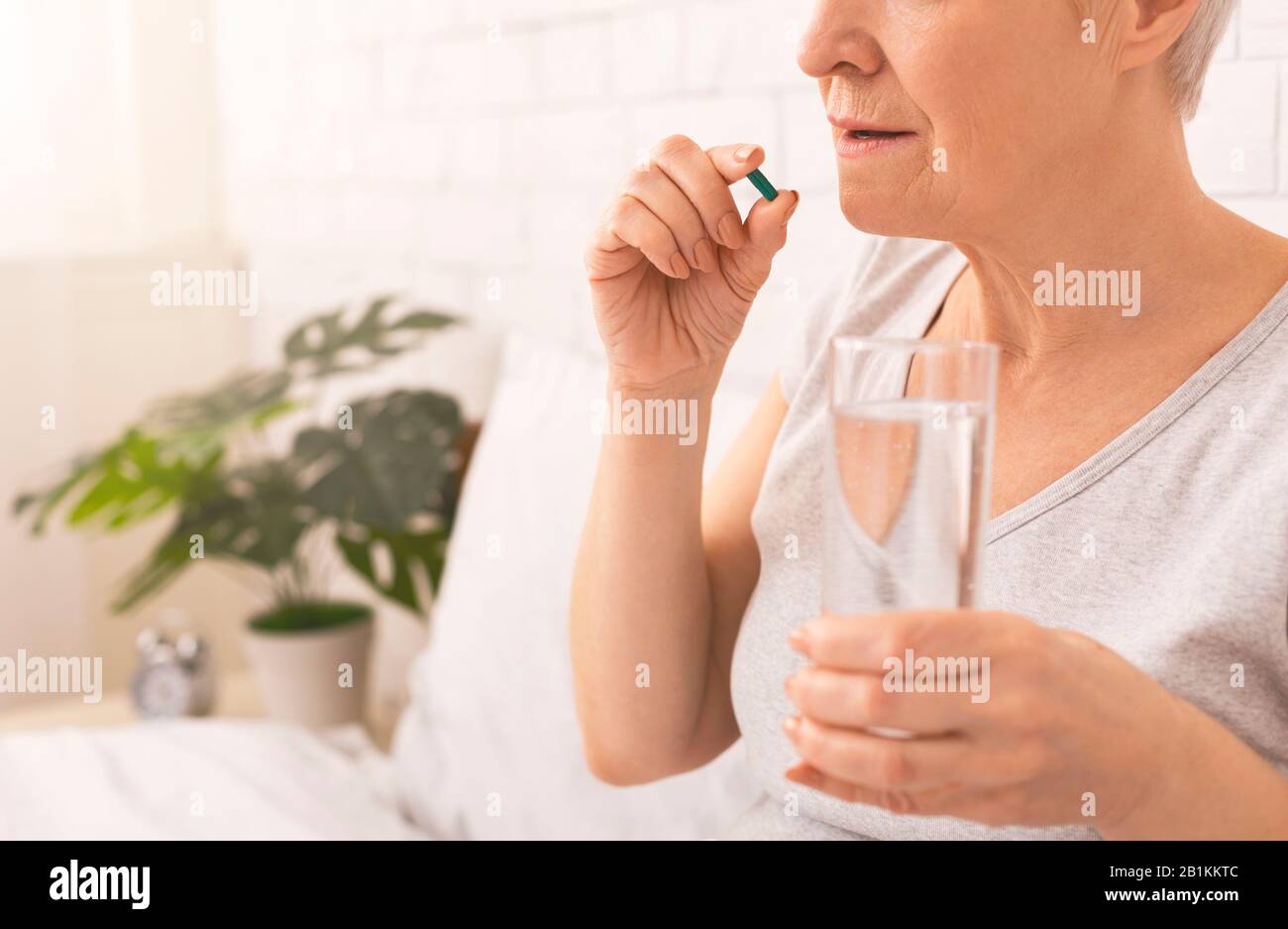 Healthy senior lady taking pills with glass of water in bed Stock Photo ...