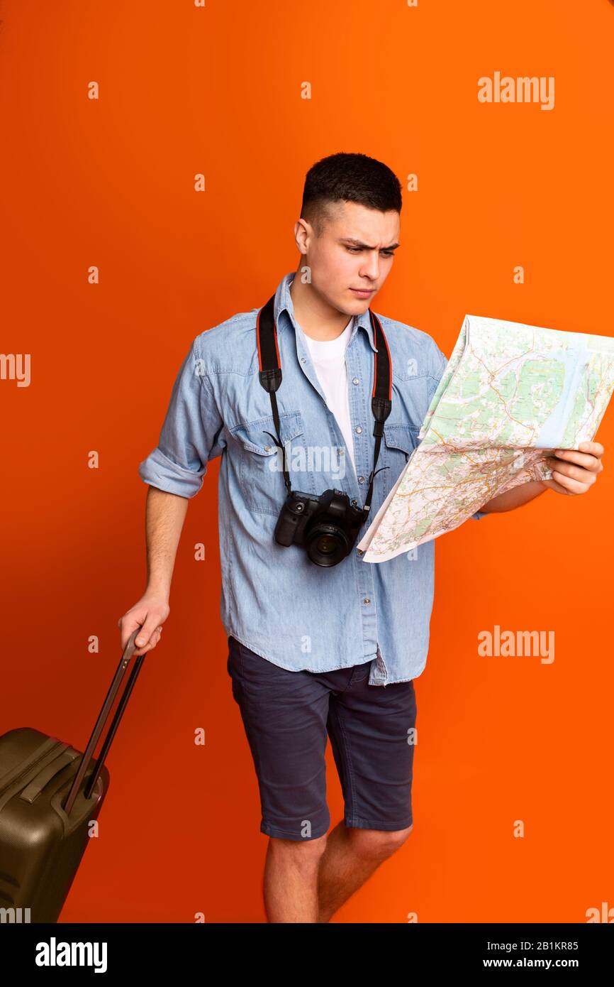 Confused tourist with camera and luggage looking at map Stock Photo - Alamy