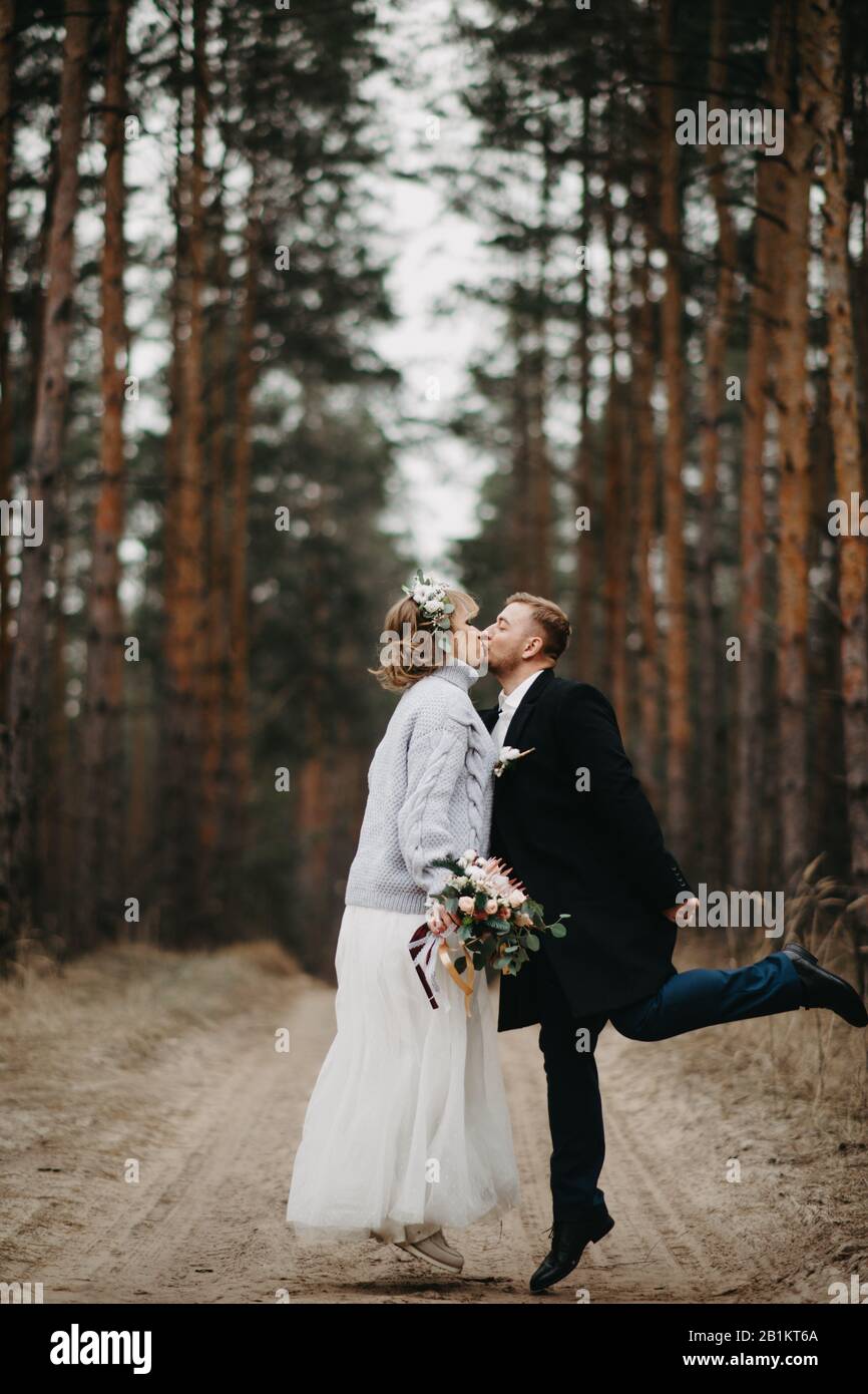 Newlyweds have a fun, jump and kiss at forest path in a coniferous ...