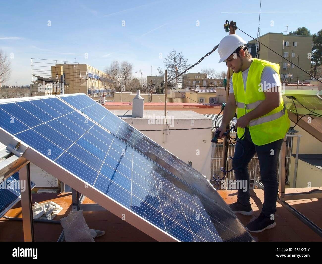 Caucasian attractive young technician cleaning solar panels with a hose ...