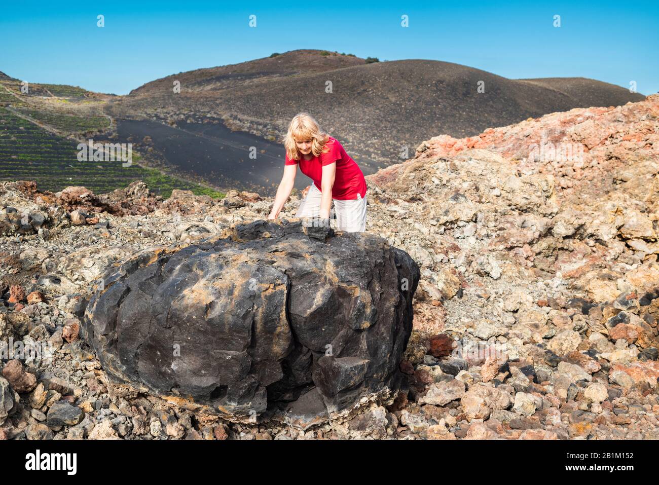 A female tourist examines a large vesicular basaltic lava volcanic bomb ...