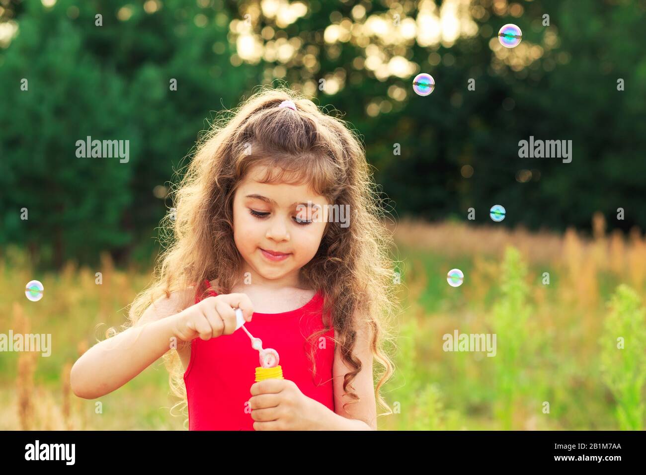 Cute Little Girl blowing soap bubbles at the field at summer day ...