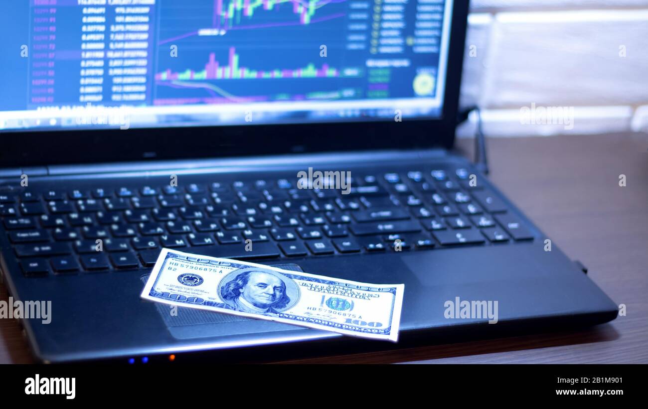 a hundred-dollar bill is placed on a laptop with a price chart for ...