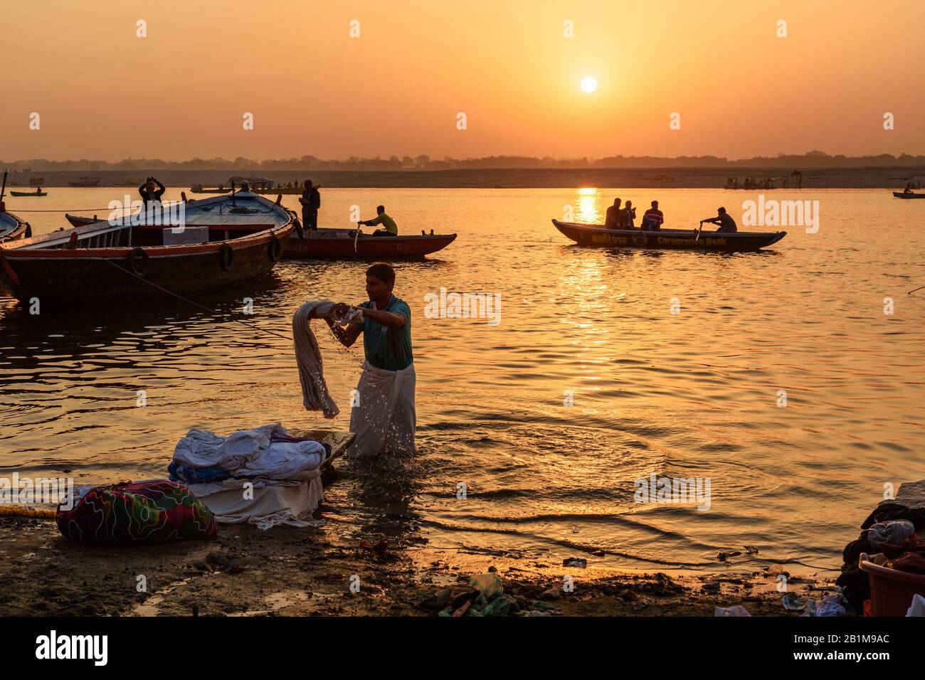 Indian man washing clothes in holy water of river Ganga in sunrise ...