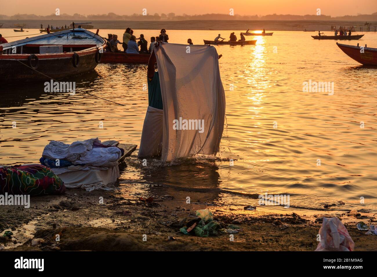 Indian man washing clothes in holy water of river Ganga in sunrise ...