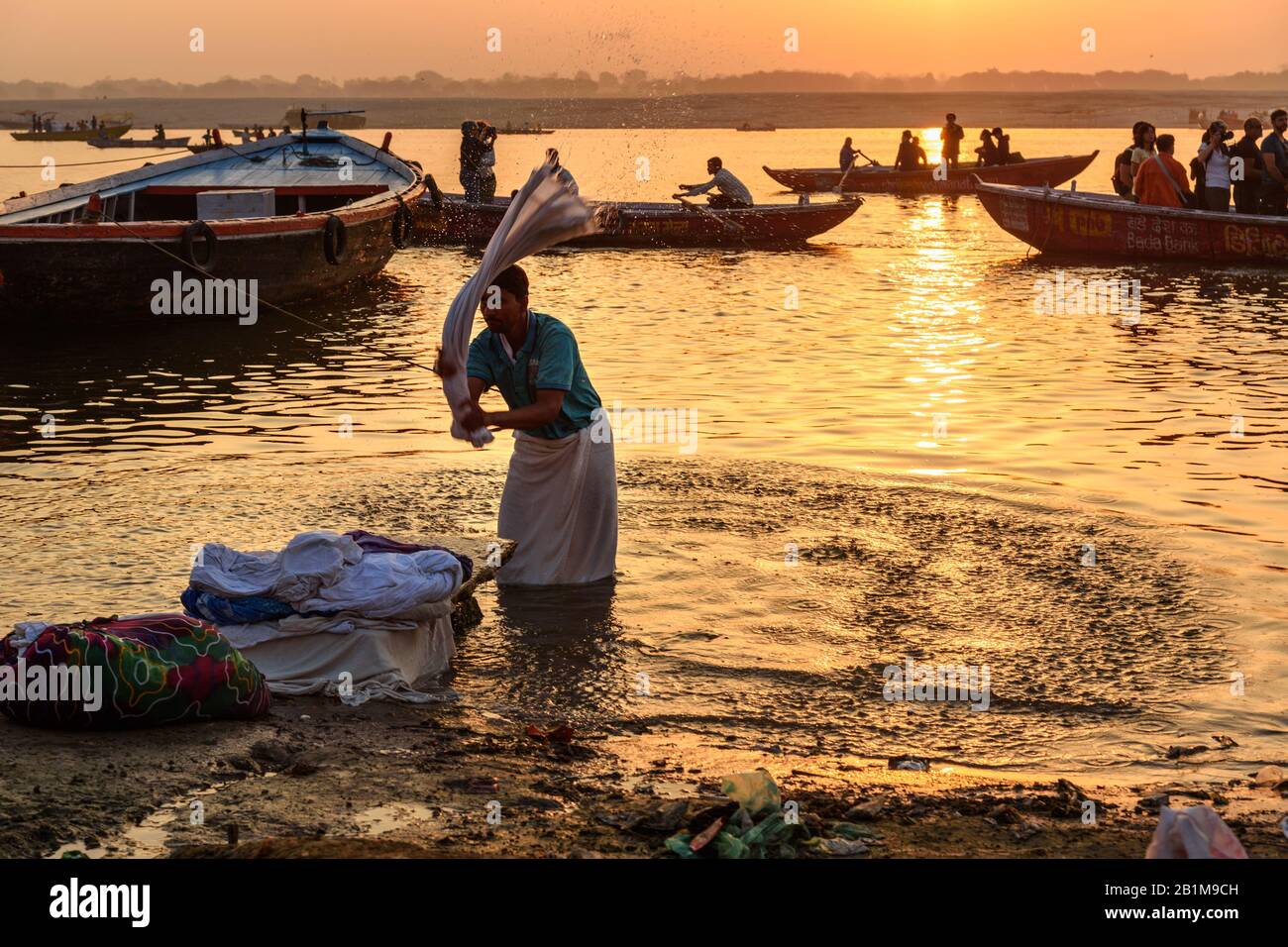 Indian man washing clothes in holy water of river Ganga in sunrise ...