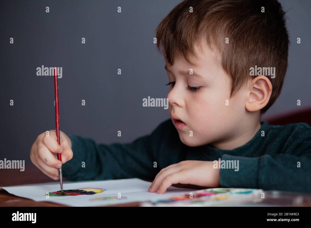 Little boy draws a brush and paint his first picture. Closeup portrait ...