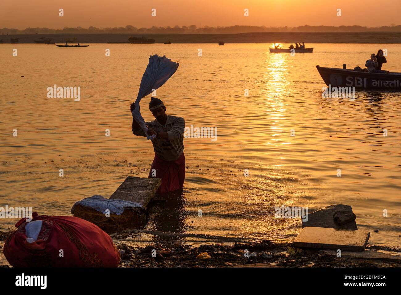 Indian man washing clothes in holy water of river Ganga in sunrise ...
