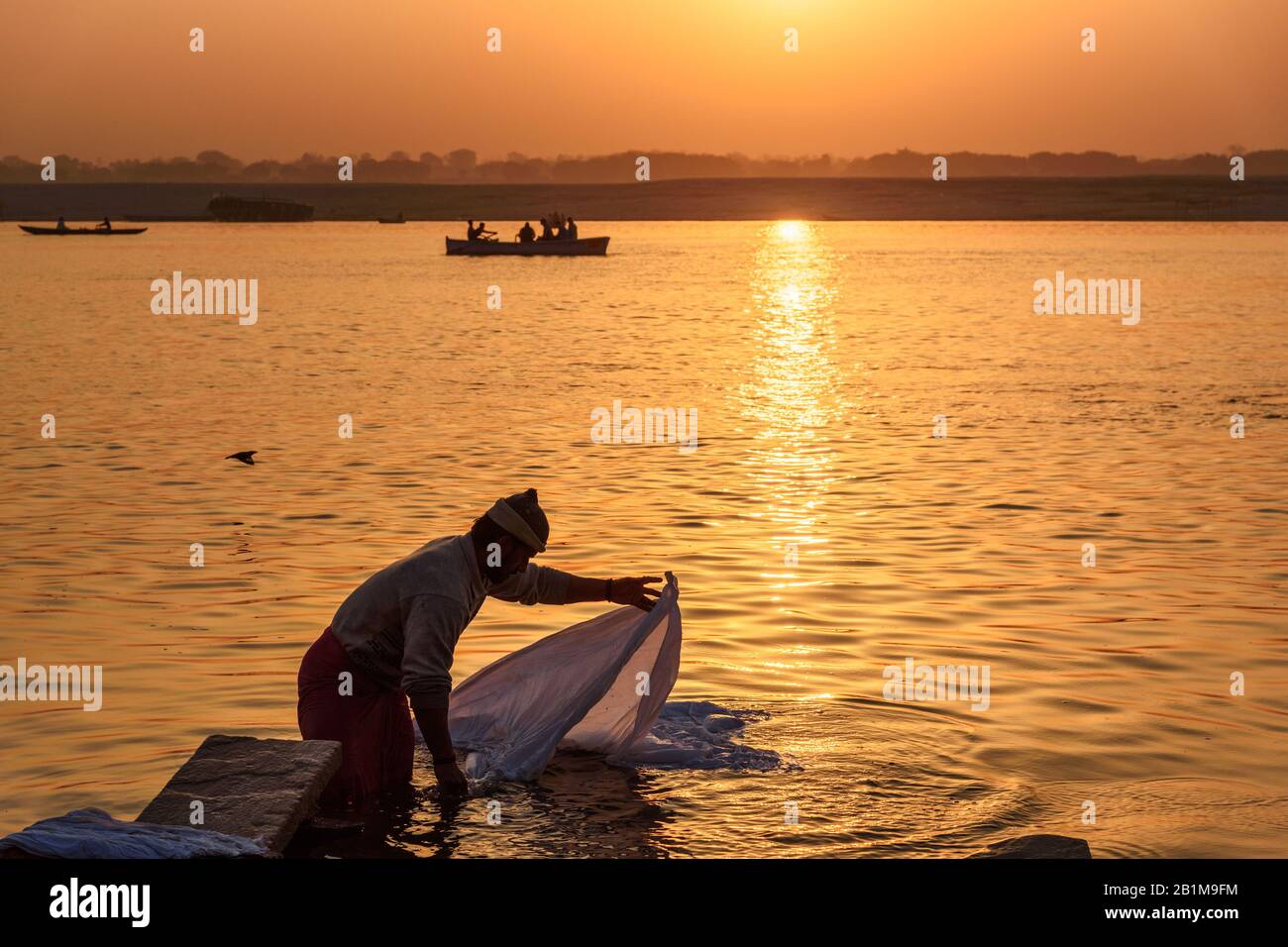 Indian man washing clothes in holy water of river Ganga in sunrise ...