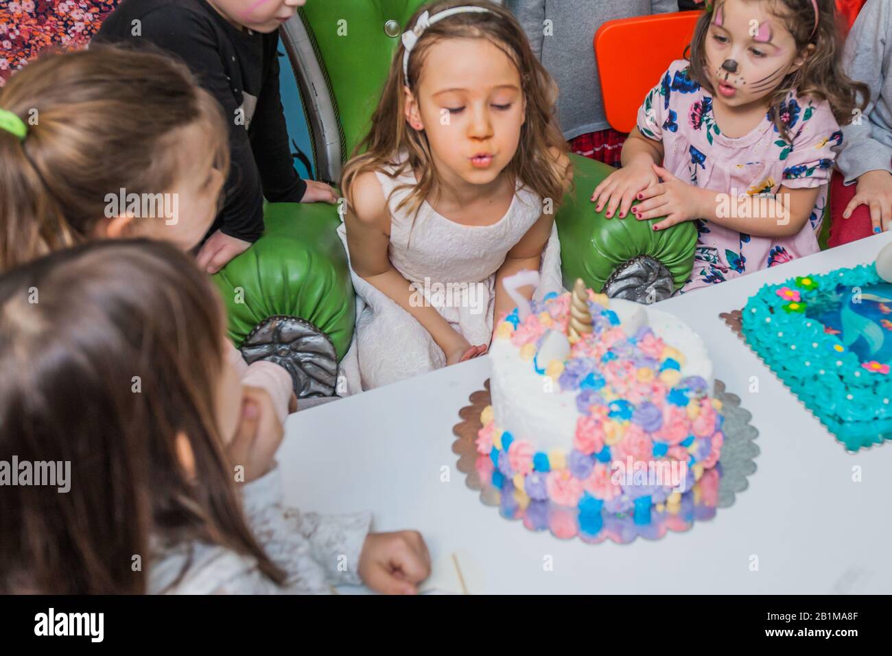 Little Girl Blowing Out Candle On Birthday Cake At Party In Playroom ...
