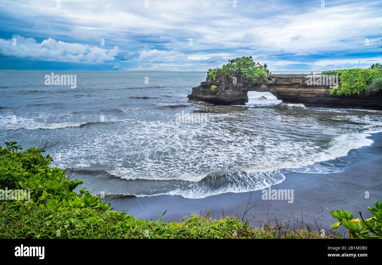 Batu Bolong Temple on a rock peninsula forming a natural bridge at the ...