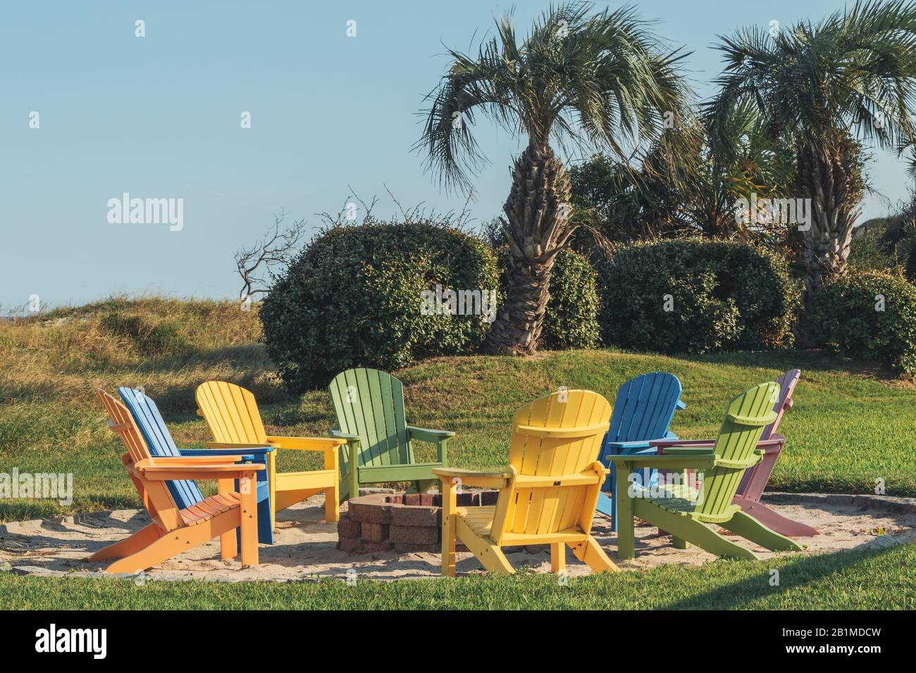 Colorful beach charis around a fire pit on the beach dunes with palm ...