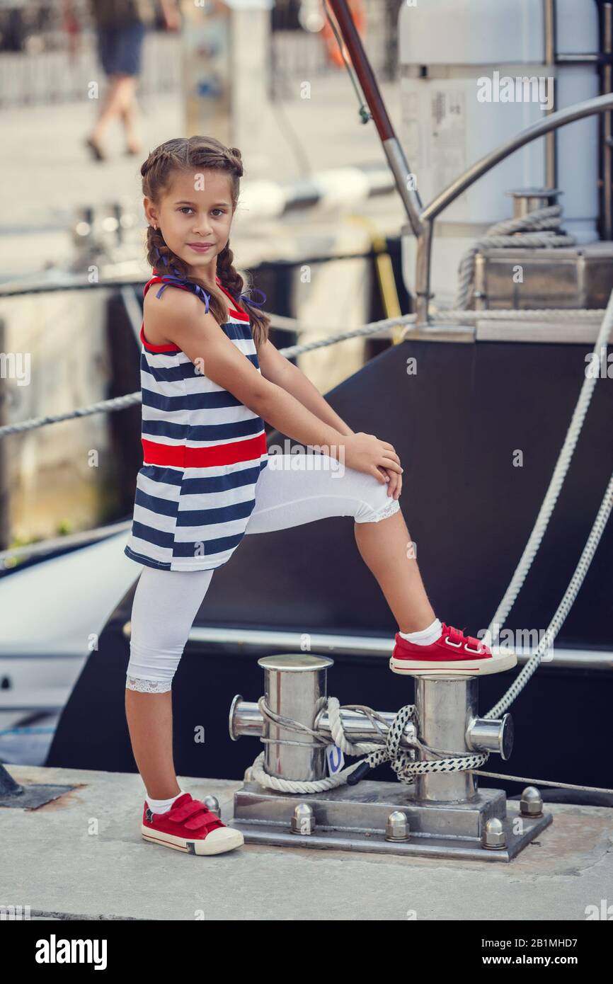 A beautiful little girl in a marine style against the backdrop of boats ...