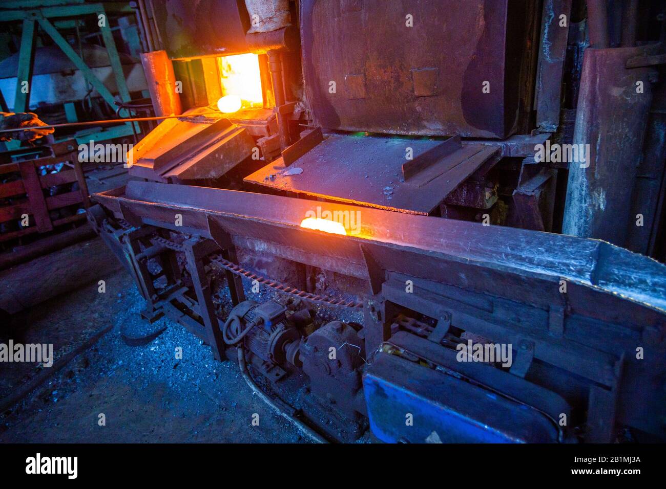 A process of moving luminous hot steel workpiece from furnace to hammer ...