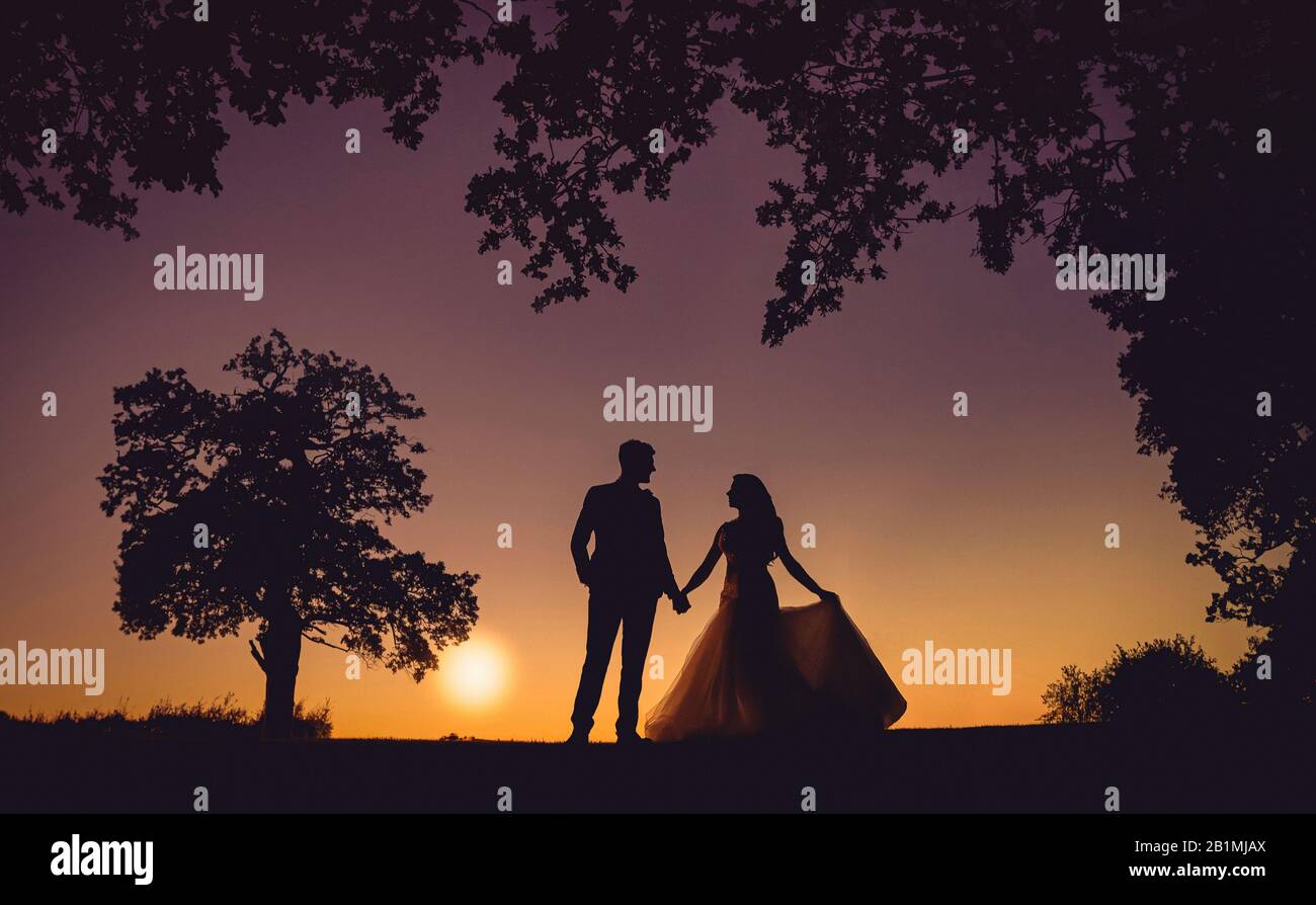 Bride and groom at sunset with the setting sun behind. Orange and ...