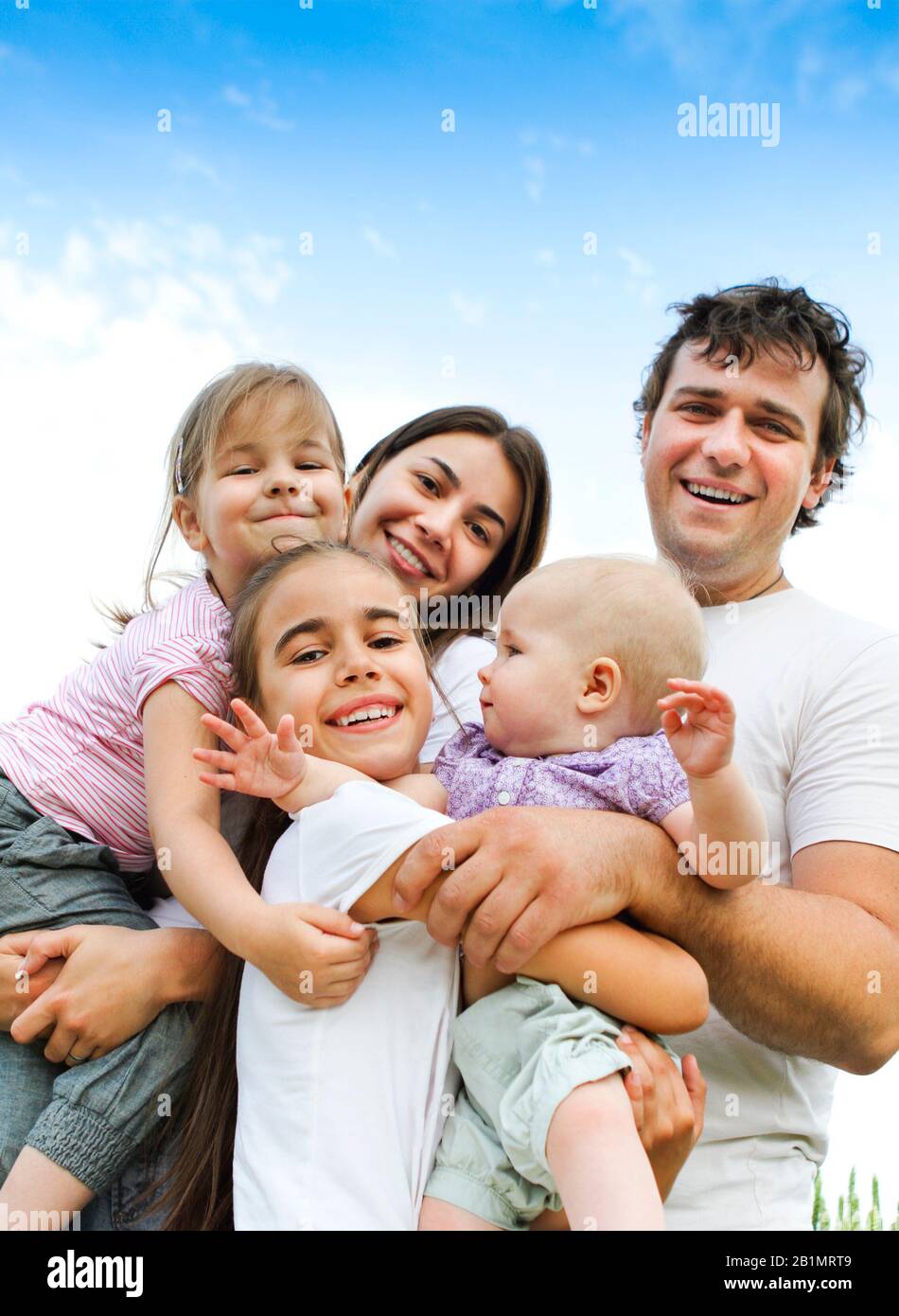 Happy family of parents and three girls hugging and smiling at camera ...