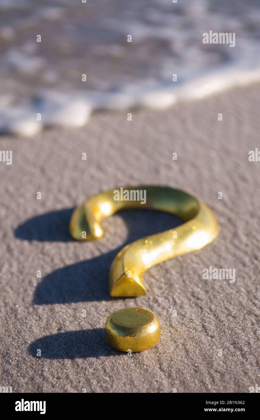 Gold question mark shining outdoors on the beach next to a wave on ...